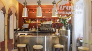 Interior de restaurante com área de bar, banquetas e luminárias pendentes.