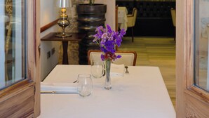 Mesa de jantar posta com um vaso de flores roxas, uma luminária e dois copos.