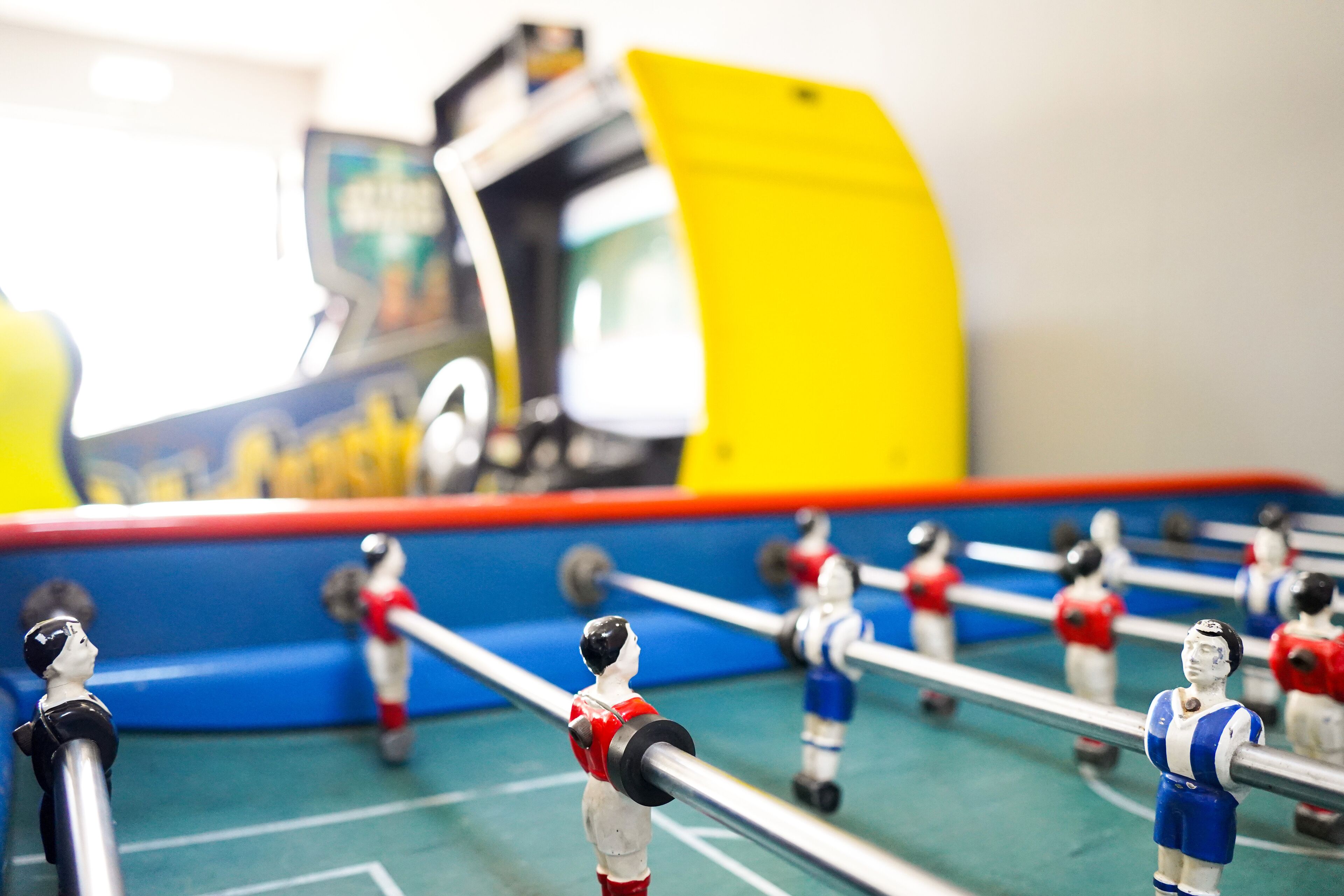 Uma mesa de futebol de mesa com vários jogadores e uma mesa de pingue-pongue ao fundo.