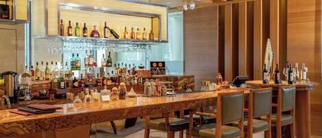 Uma área de bar com um balcão comprido, vários bancos e uma variedade de garrafas e copos.