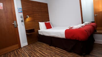 Quarto de hotel com piso de madeira, cama com roupa de cama branca e vermelha, cabeceira de madeira e um espelho na parede.