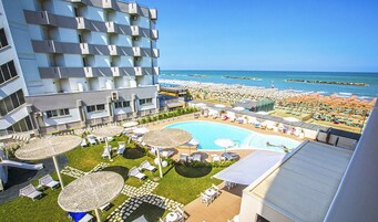 Um hotel com área de piscina, vista para a praia e várias varandas.