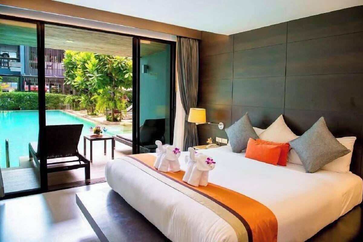 Quarto de hotel com uma cama grande, vista para uma piscina e uma pequena mesa com abajur.