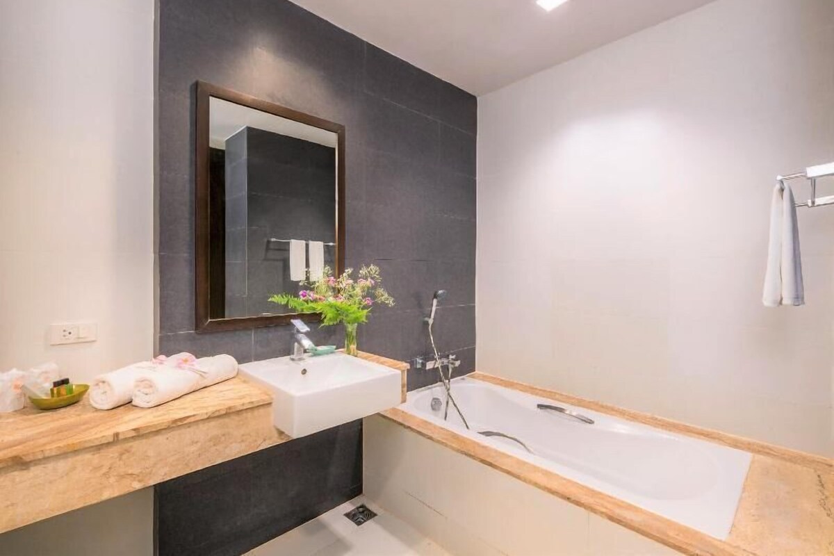 Uma casa de banho moderna com um espelho grande, uma pia, uma banheira e um porta-toalhas.