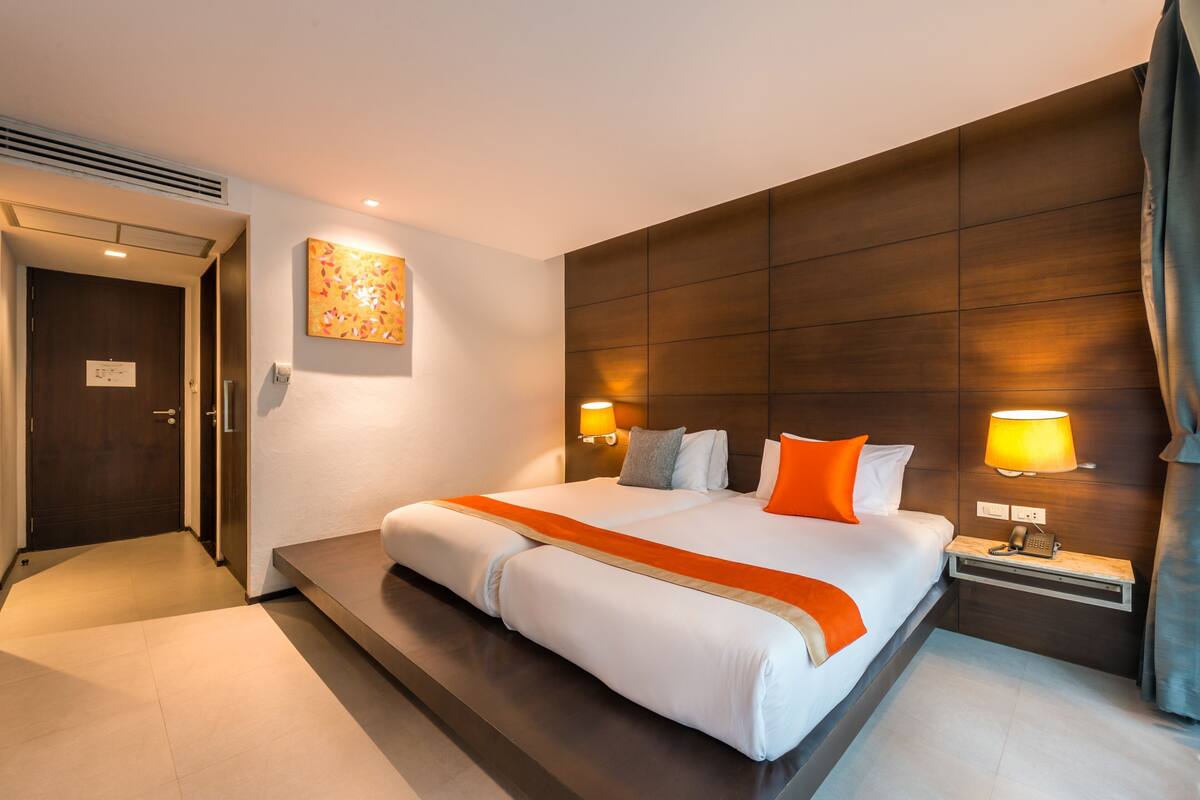 Quarto de hotel com uma cama grande, abajures, mesa de cabeceira e porta.