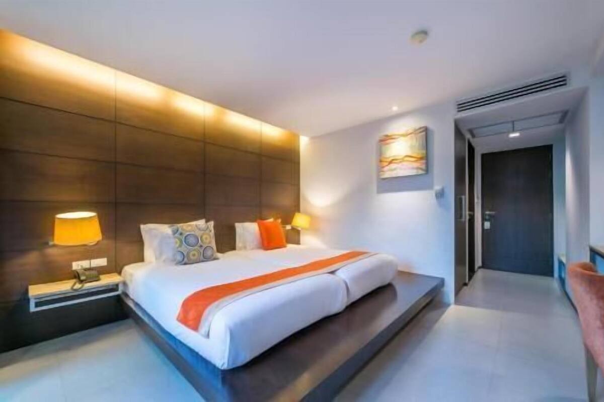 Quarto de hotel moderno com uma cama grande, uma mesa de cabeceira, um abajur e um quadro na parede.
