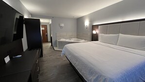 Quarto de hotel com cama grande, escrivaninha, televisão, banheiro com banheira e espelho.