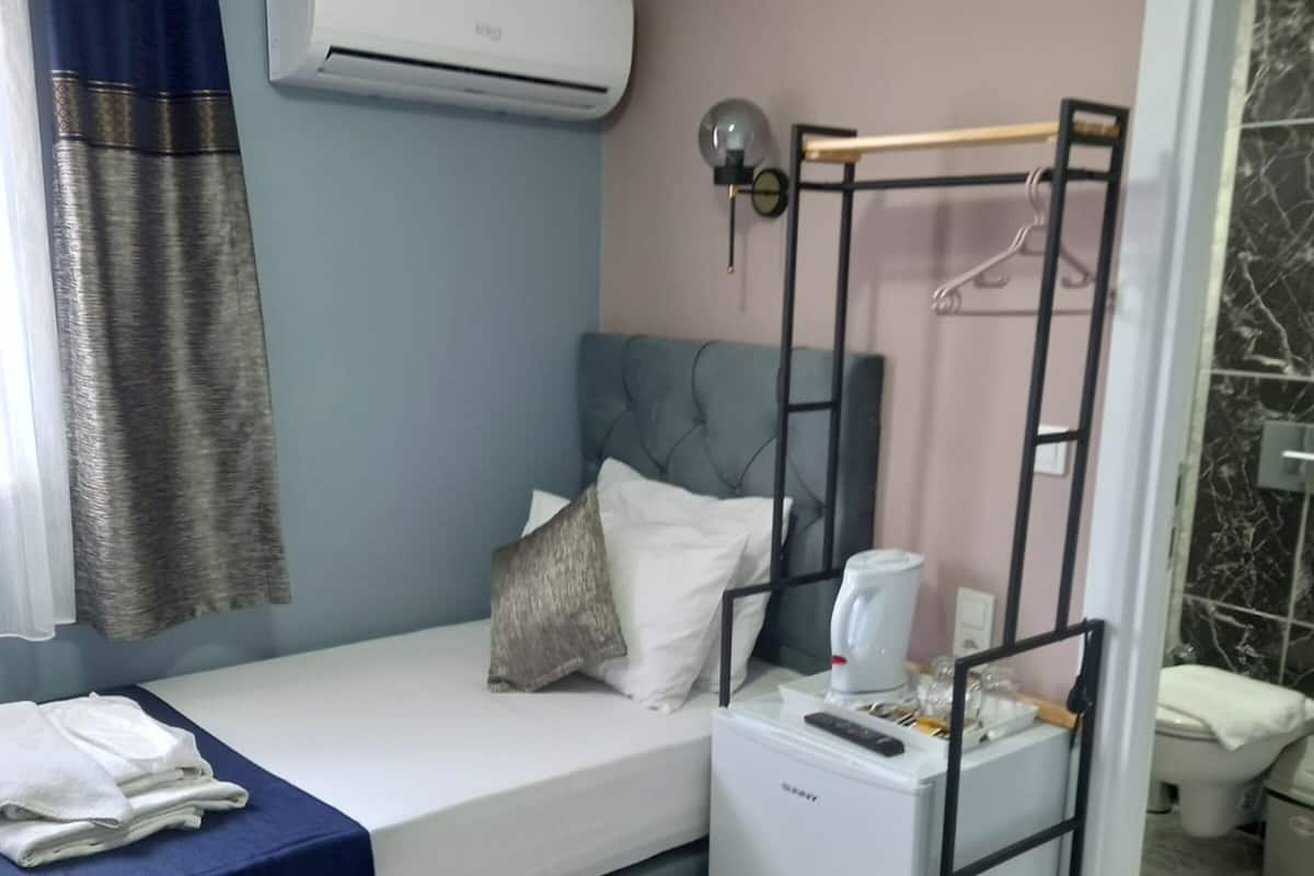 Quarto compacto com uma cama de solteiro, mesa de cabeceira, guarda-roupa e ar condicionado.