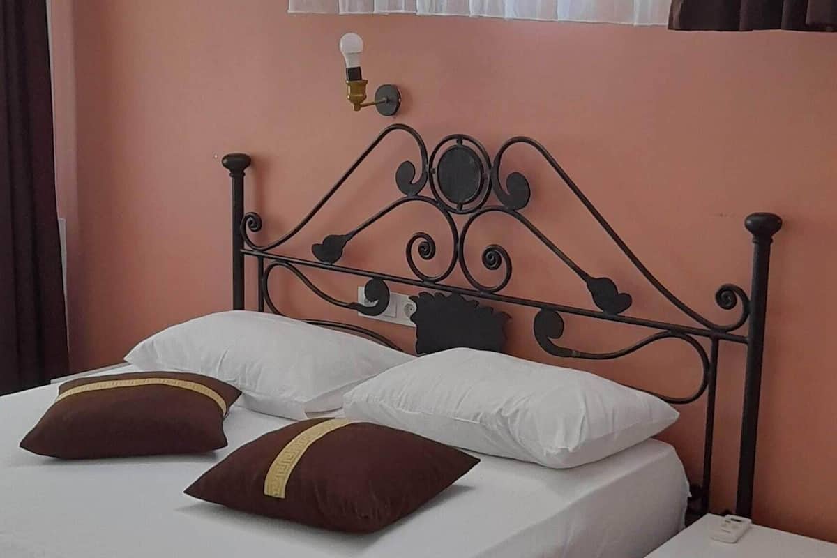 Uma cama bem arrumada com um cobre-leito estampado, uma mesinha de cabeceira e um criado-mudo.