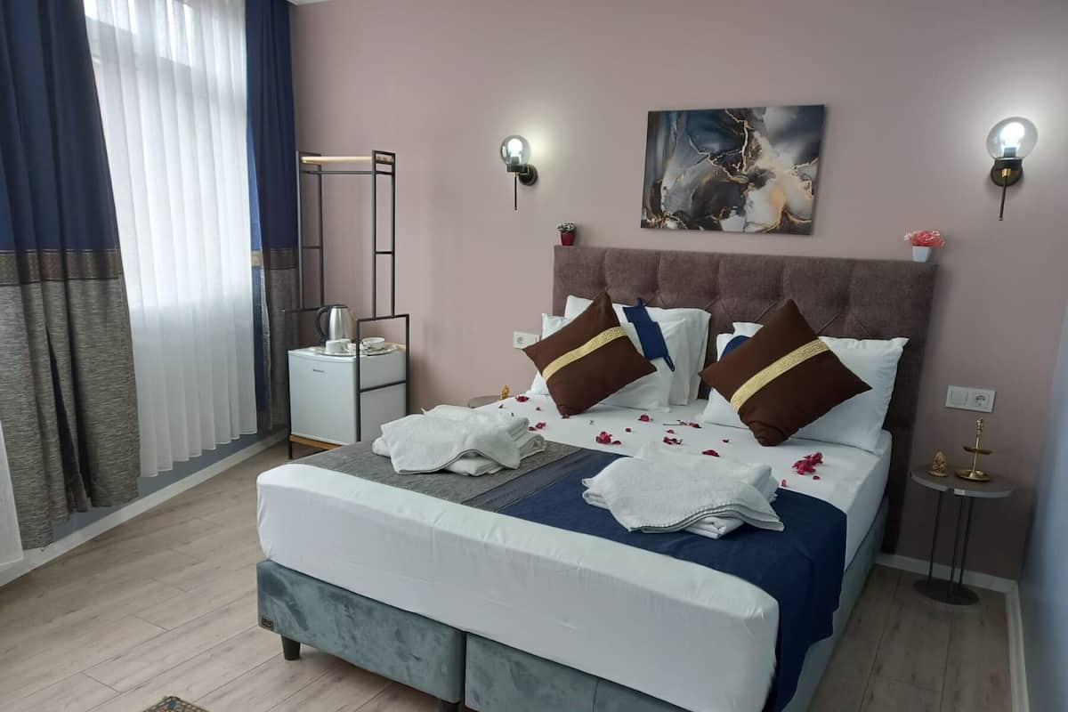 Uma cama bem arrumada com travesseiros, uma mesinha de cabeceira com abajur, uma obra de arte na parede e uma pequena mesa com um objeto decorativo.