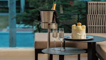 Uma mesa com um bolo, duas taças de champanhe, um balde de metal com uma garrafa, e vista para uma piscina e vegetação.
