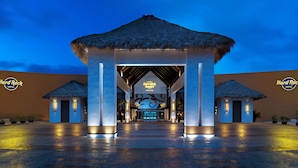 Entrada do Hard Rock Hotel com estrutura de telhado de palha, sinalização iluminada e plantas em vasos.