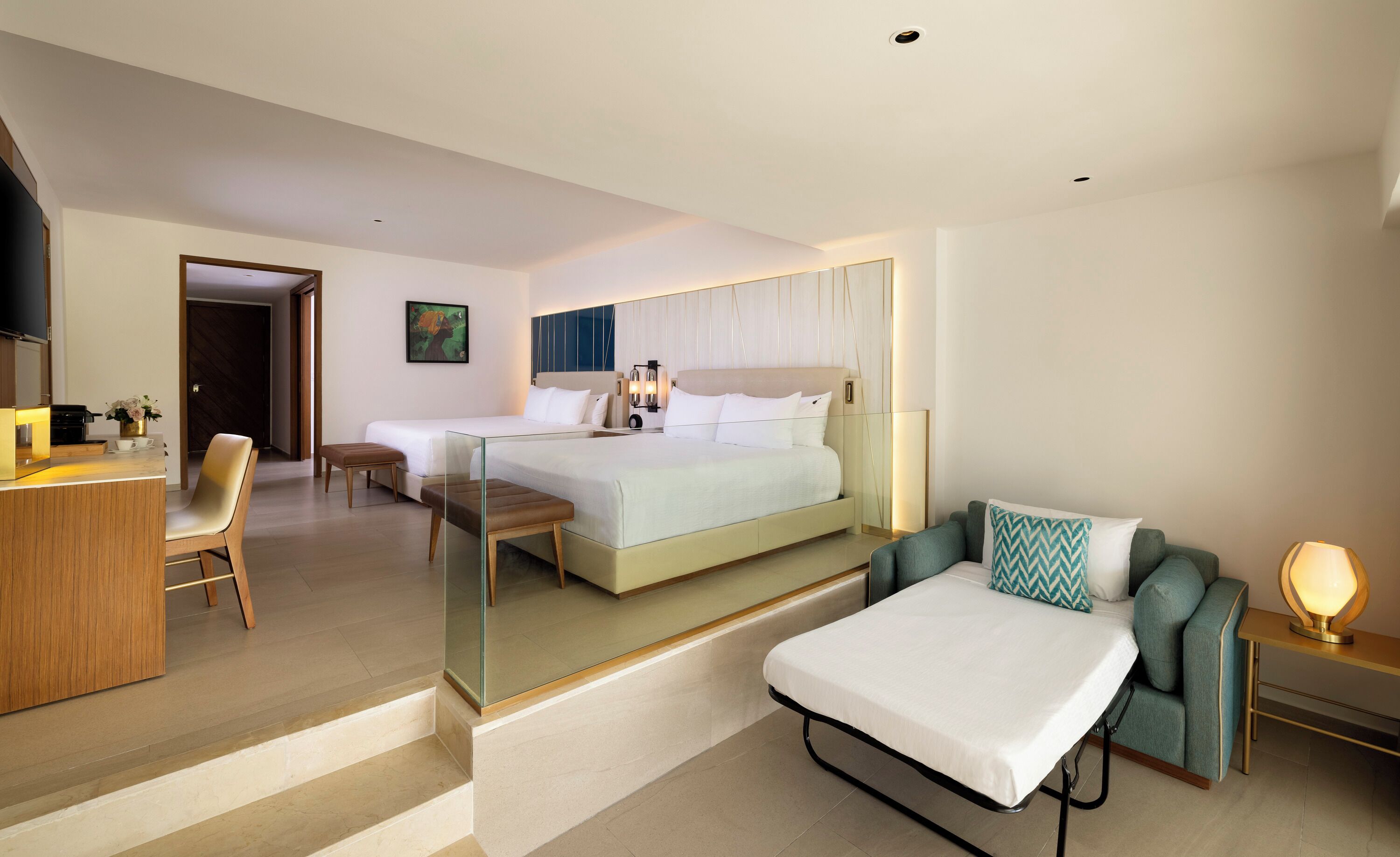Quarto de hotel moderno com cama, sofá, escrivaninha e divisória de vidro.
