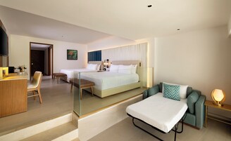 Quarto de hotel moderno com cama, sofá, escrivaninha e divisória de vidro.