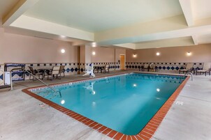 Piscina interior com borda em azulejo, sala de trocas e área de estar com cadeiras e mesas.