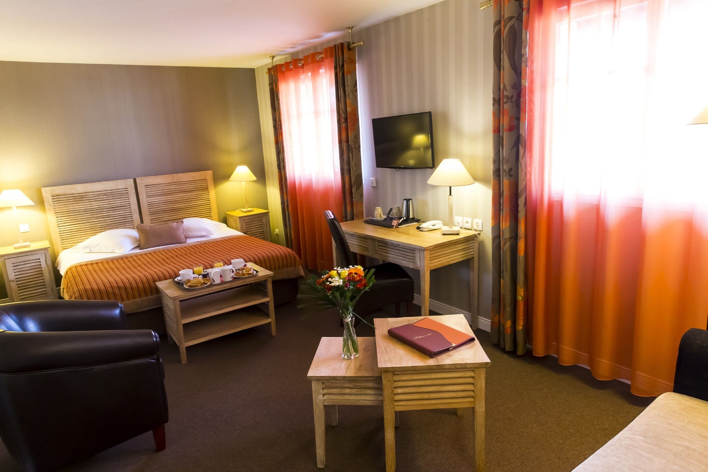 Quarto de hotel com cama, escrivaninha, cadeira e uma mesinha com um vaso de flores.