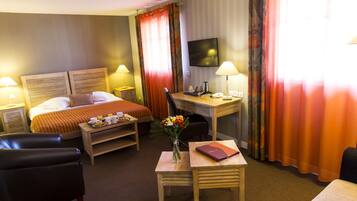 Quarto de hotel com cama, escrivaninha, cadeira e uma mesinha com um vaso de flores.