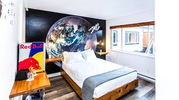 Quarto com um grande mural de globo na parede, uma cama com estrutura de madeira, uma pequena mesa com o logotipo Red Bull e uma janela com vista para o exterior.