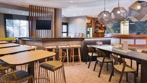 Um restaurante moderno com mesas e cadeiras de madeira, um espaço de bar e uma televisão de tela plana na parede.