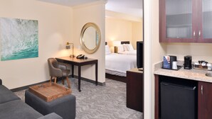 Quarto de hotel com área de estar, escrivaninha, cama, mini-geladeira e cafeteira.