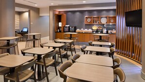 Um restaurante moderno com várias mesas e cadeiras, um balcão de café e uma televisão de tela plana na parede.