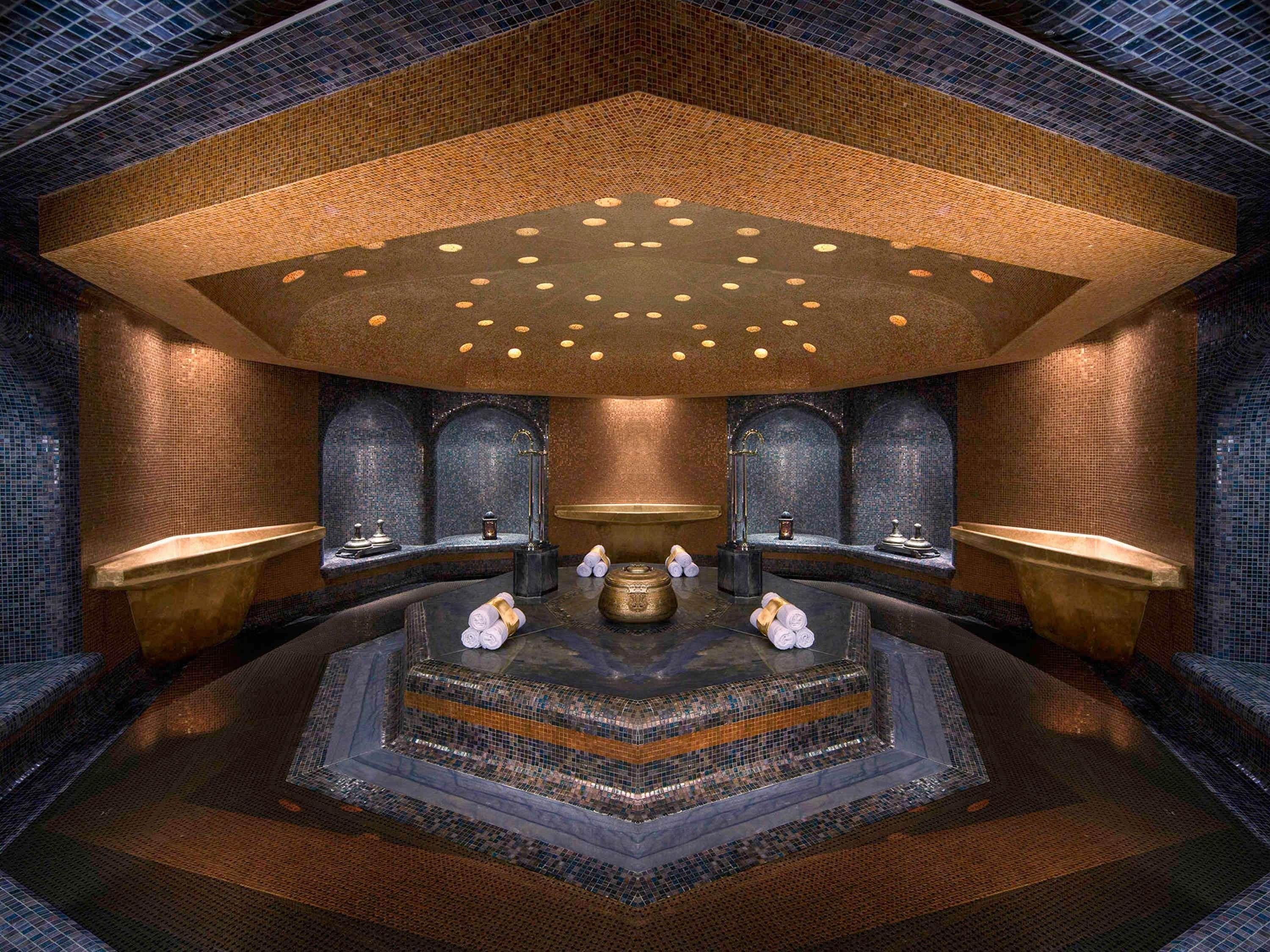 Um spa luxuoso com banheira de hidromassagem central, vários espaços para relaxar e teto decorativo.