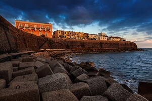 Uma cidade costeira com edifícios ao longo do penhasco, um molhe rochoso e o mar.