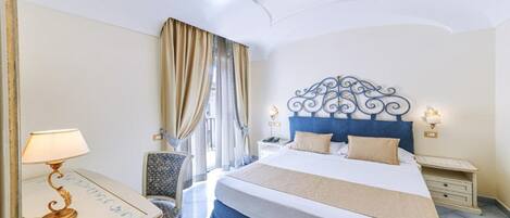 Quarto de hotel com uma cama grande, uma escrivaninha com abajur, uma cadeira e uma janela com cortinas.