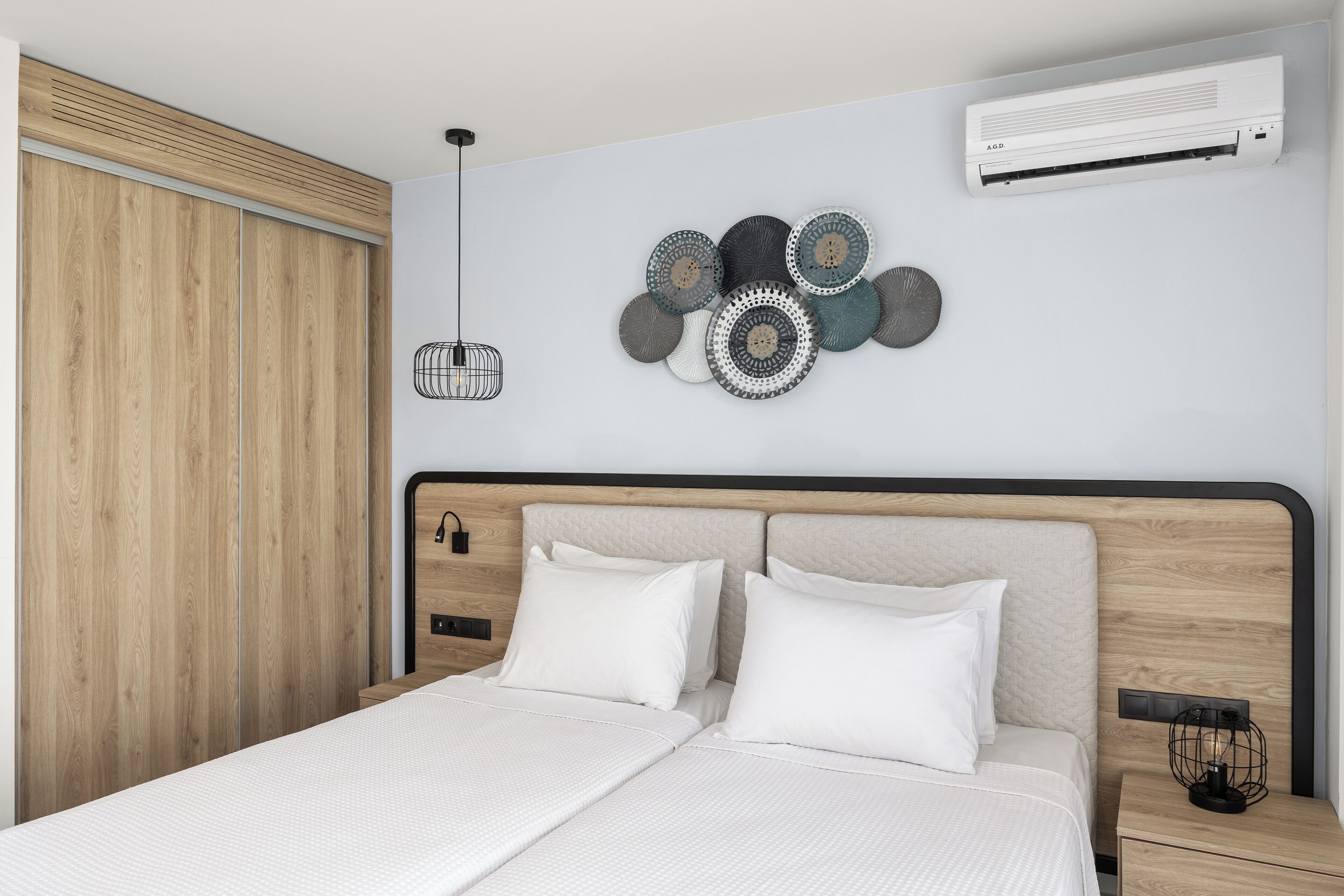 Um quarto moderno com um guarda-roupa de madeira, uma cama com roupa de cama branca, um ar condicionado fixado na parede e arte decorativa na parede.