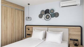 Um quarto moderno com um guarda-roupa de madeira, uma cama com roupa de cama branca, um ar condicionado fixado na parede e arte decorativa na parede.