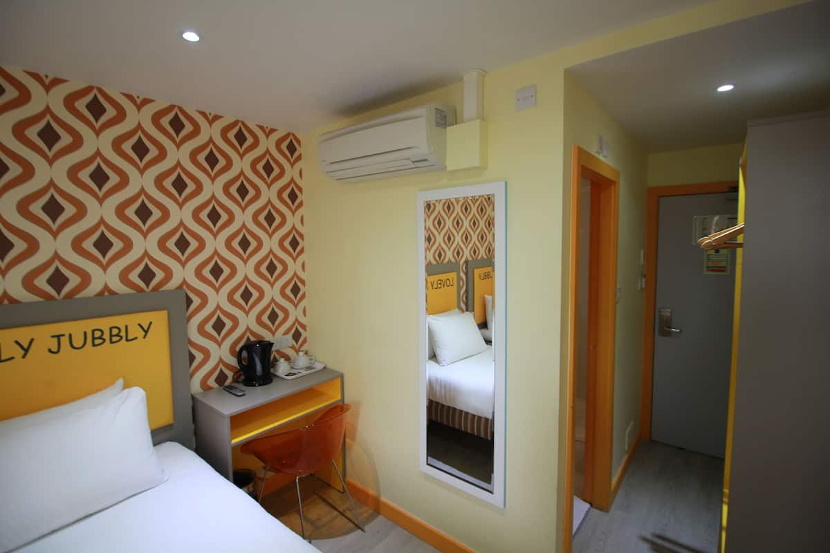 Quarto de hotel com cama, escrivaninha, cadeira, ar condicionado e espelho.