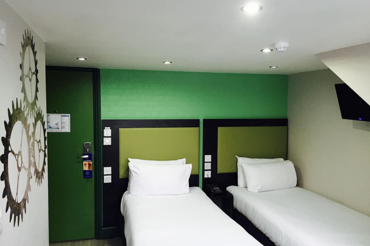 Quarto de hotel com duas camas de solteiro, paredes verdes e um lustre.