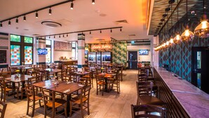 Um restaurante com várias mesas e cadeiras de madeira, um espaço de bar e um letreiro que diz 'Lovely Jubbly'.
