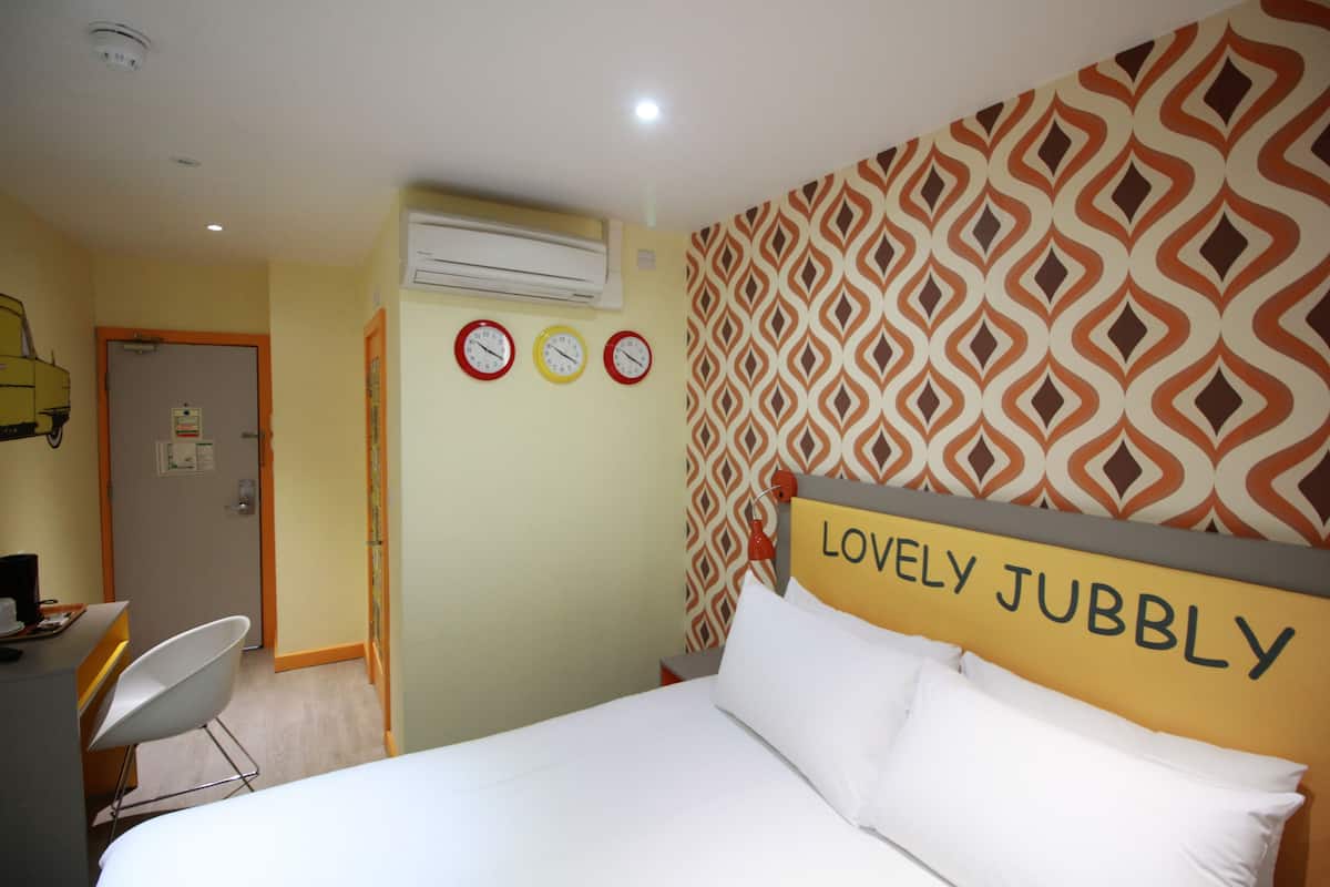 Quarto de hotel com uma cama, uma escrivaninha com cadeira e parede estampada.