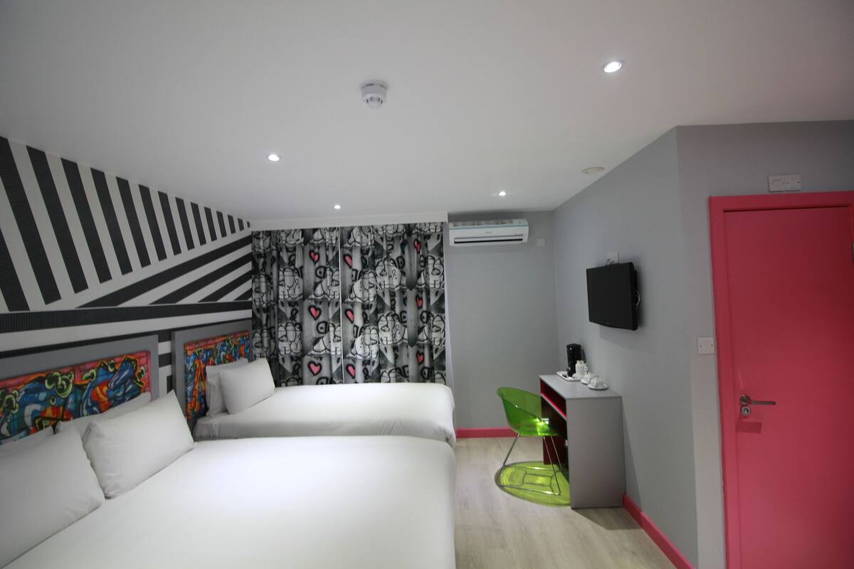 Quarto de hotel com duas camas, uma escrivaninha, uma cadeira, uma televisão e uma porta vermelha.