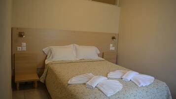 Cama bem arrumada com colcha florida, cabeceira de madeira e duas luminárias laterais.