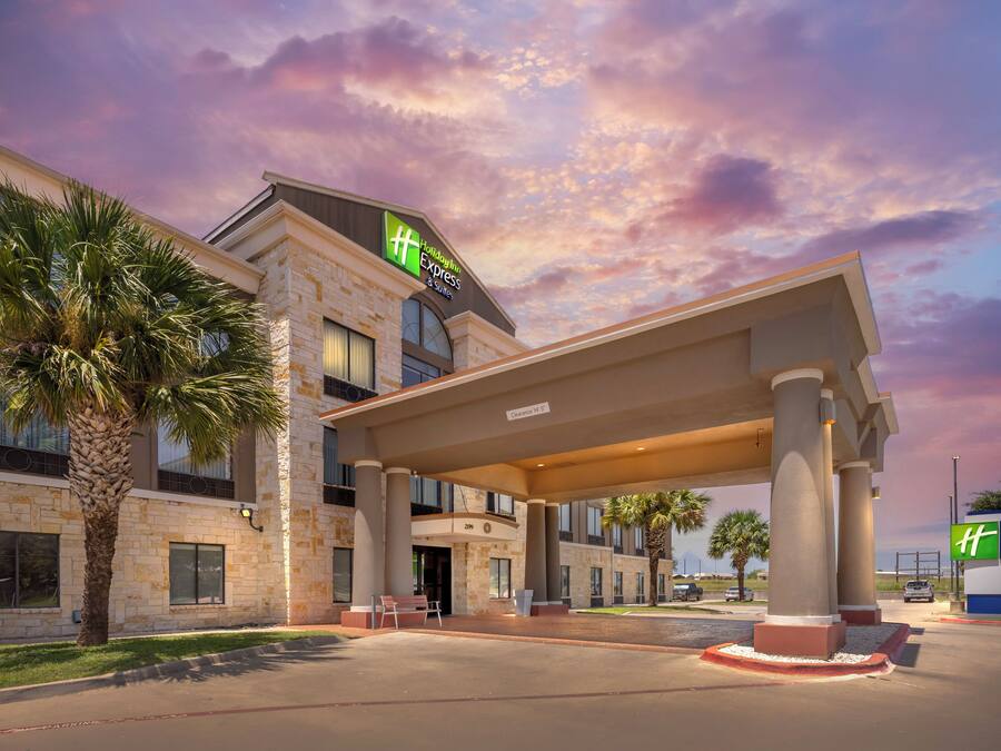 Edifício do Holiday Inn Express & Suites com fachada de pedra, entrada coberta e palmeiras.