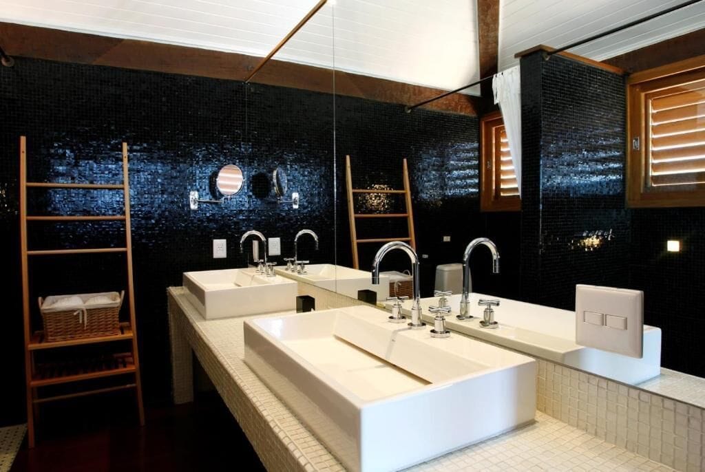 Um banheiro moderno com duas pias grandes, um espelho e uma parede de mosaico preto.