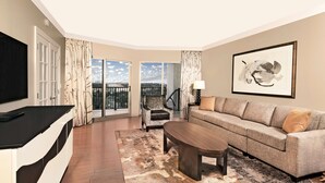 Uma sala de estar moderna com sofá, mesa de centro e televisão. Possui uma varanda com vista para a cidade.