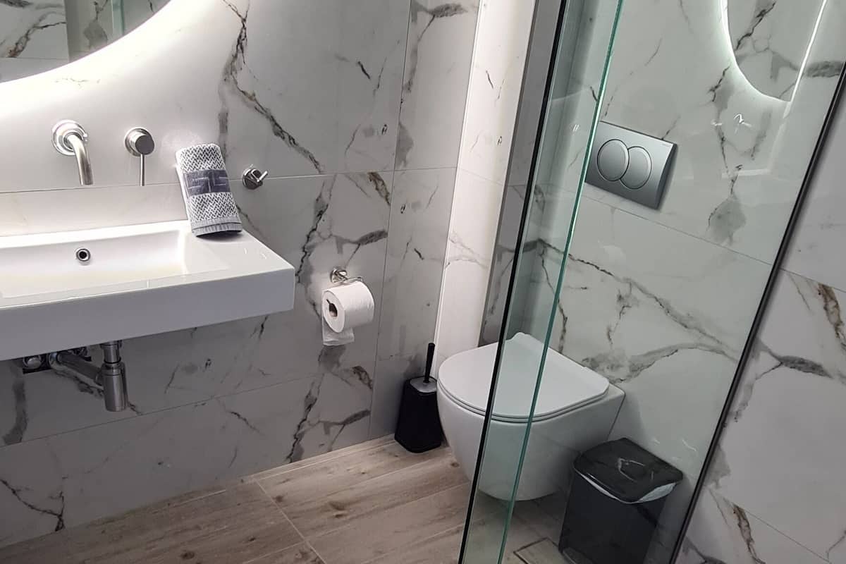 Um banheiro moderno com painel de mármore, box de vidro e piso de madeira.