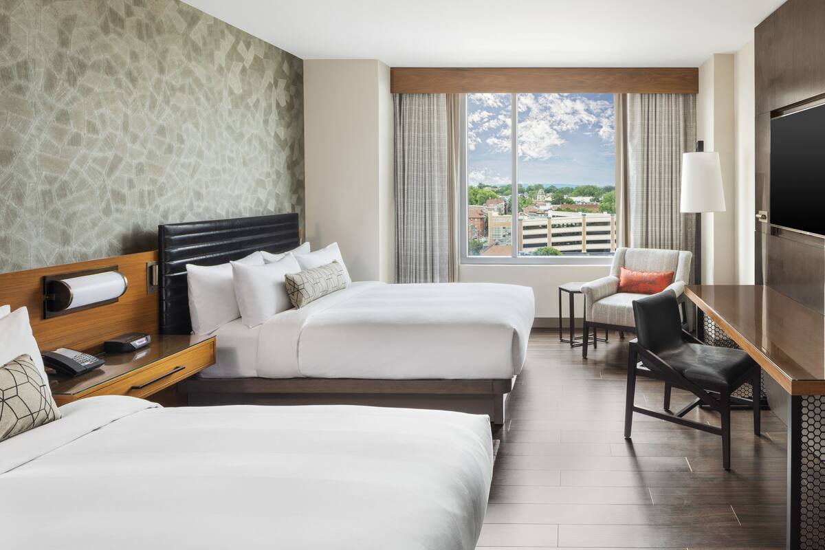 Quarto de hotel com duas camas, uma escrivaninha, uma cadeira e uma televisão.