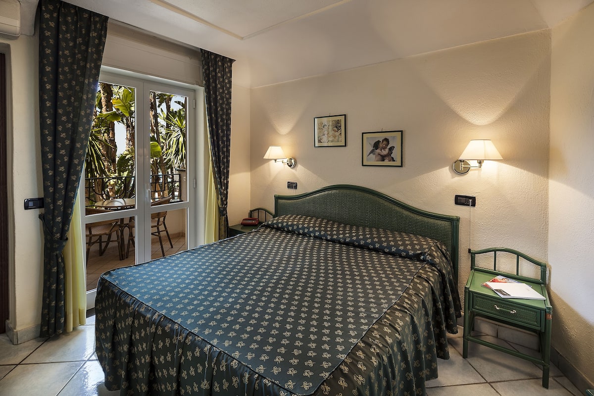 Quarto com cama, mesa de cabeceira, duas luminárias na parede e janela com cortinas.