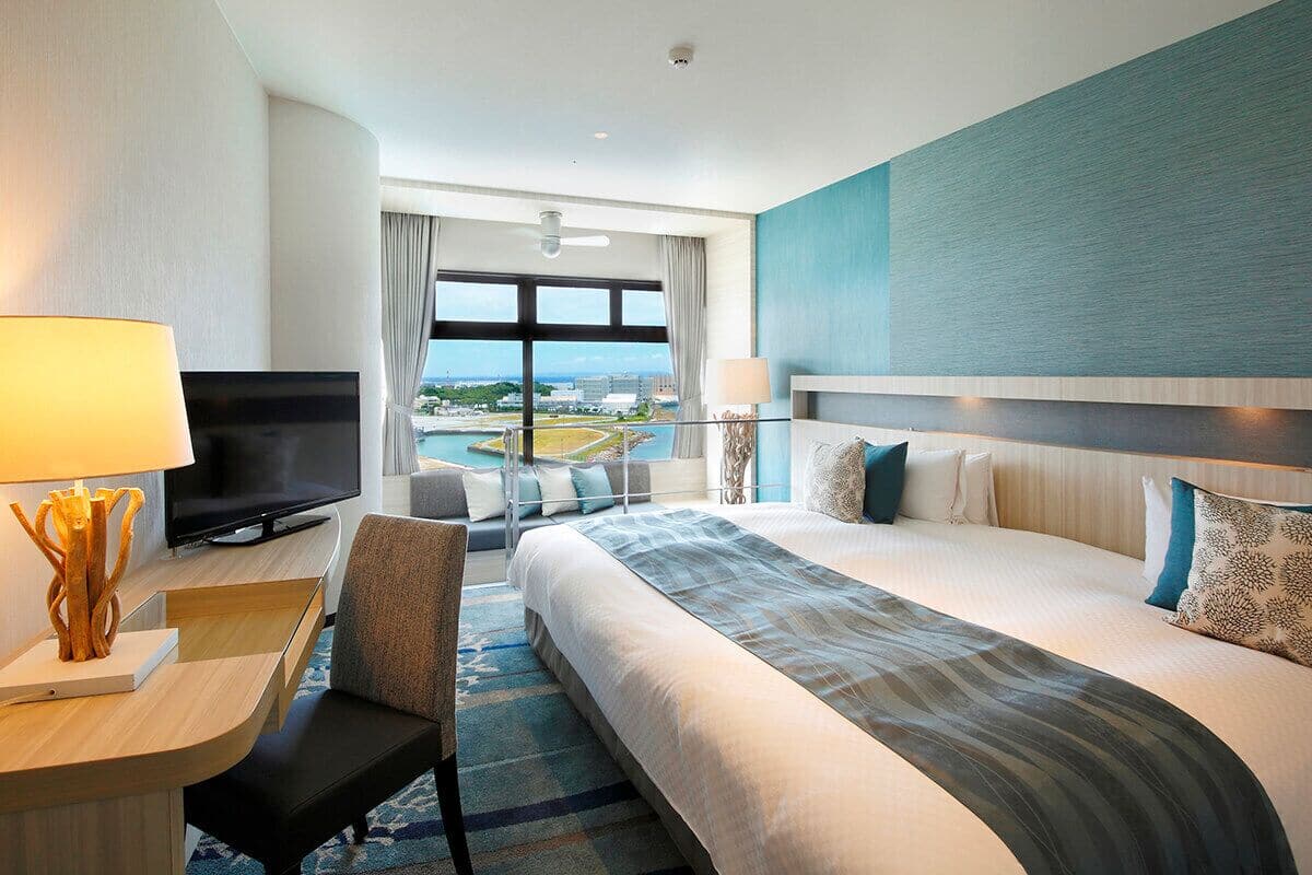 Quarto de hotel com uma cama grande, uma escrivaninha com televisão, uma cadeira e vista para a cidade.