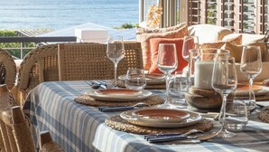 Mesa de jantar posta com pratos, copos e talheres, com vista para a água.