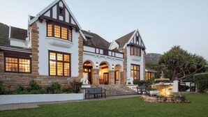 Uma casa grande de dois andares com fachada de pedra, várias janelas e um gramado bem cuidado.