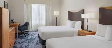 Quarto de hotel com duas camas, uma mesa, uma cadeira e uma luminária.