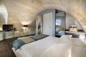 Quarto com teto de pedra, cama com roupa de cama branca, escrivaninha com computador e espelho.