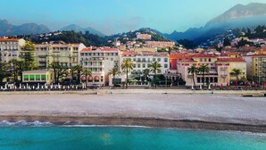 Uma cidade costeira com praia, edifícios com varandas e uma montanha ao fundo.