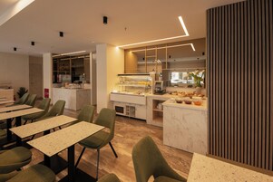 Uma área de jantar moderna com cadeiras verdes, bancada de mármore e cozinha ao fundo.