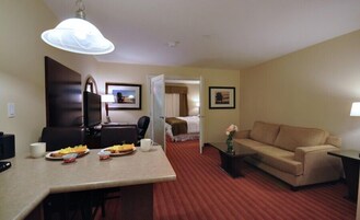Quarto de hotel com área de jantar, sofá, televisão e cama.
